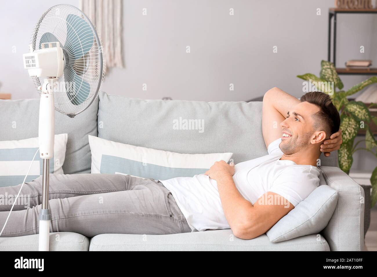 Young man using electric fan during heatwave at home Stock Photo - Alamy