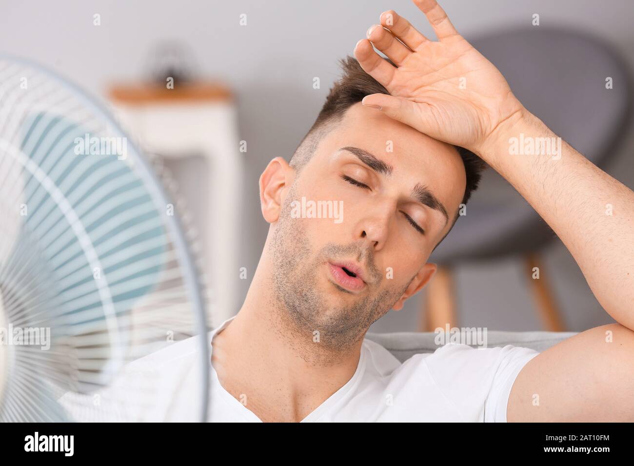 Young man using electric fan during heatwave at home Stock Photo - Alamy