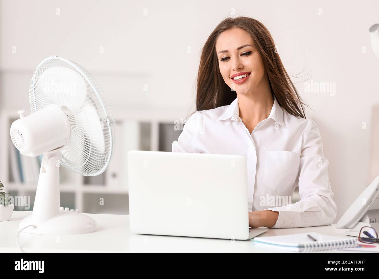 Young woman using electric fan during heatwave in office Stock Photo ...