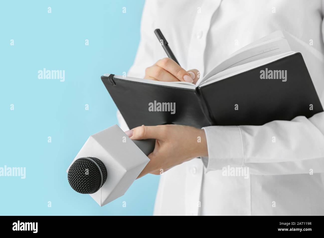 Journalist with microphone writing in notebook against color background ...