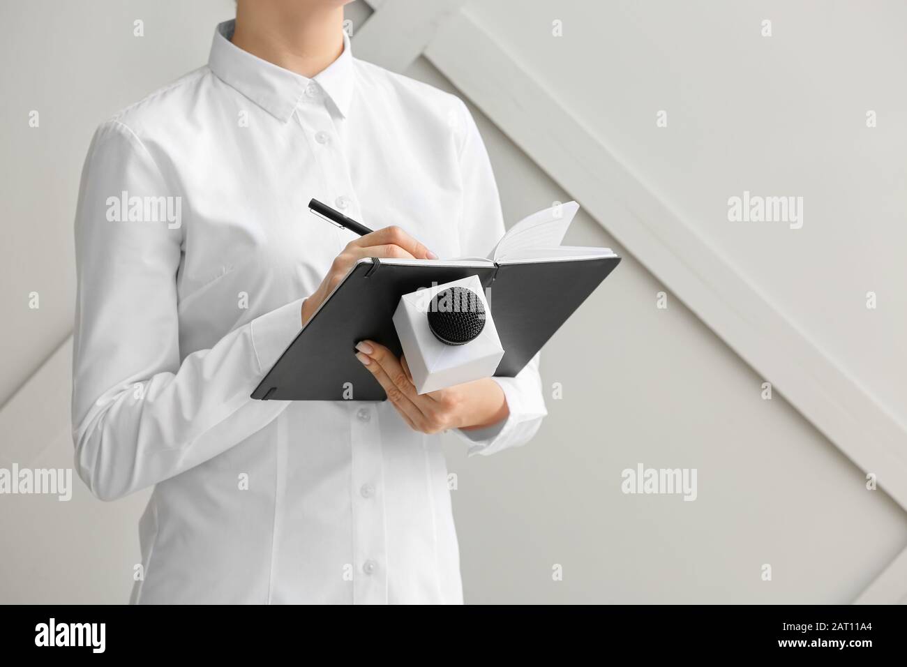 Journalist with microphone writing in notebook against grey background ...