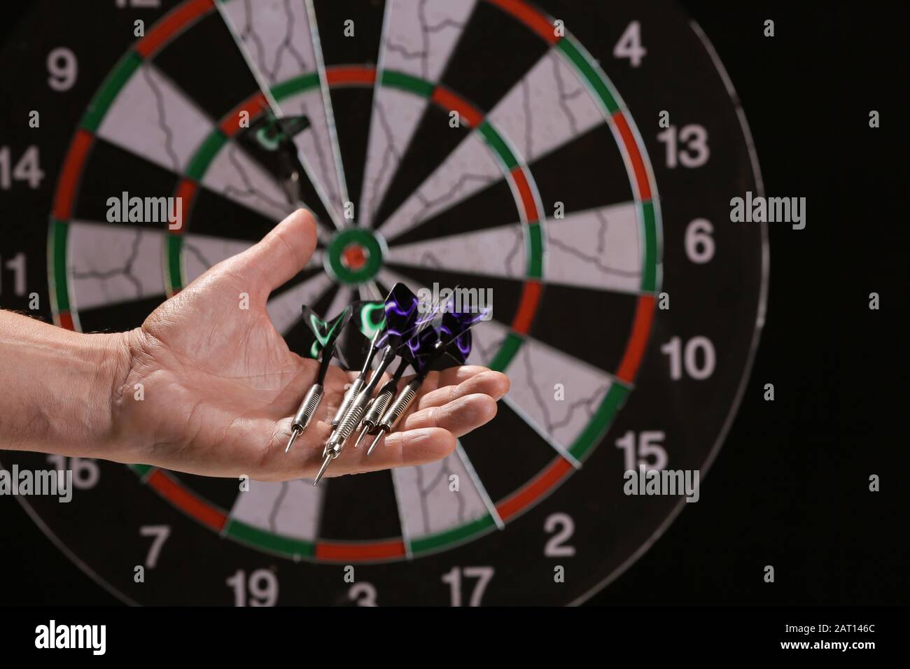 Male hand with darts and dartboard on dark background Stock Photo - Alamy