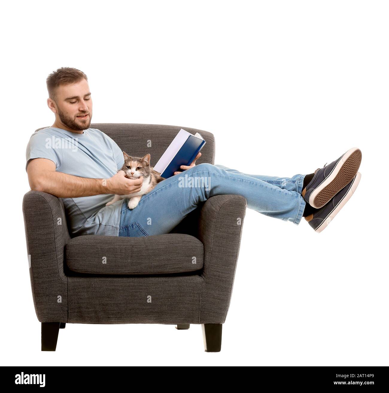 Man with cute cat reading book while sitting in armchair against white ...