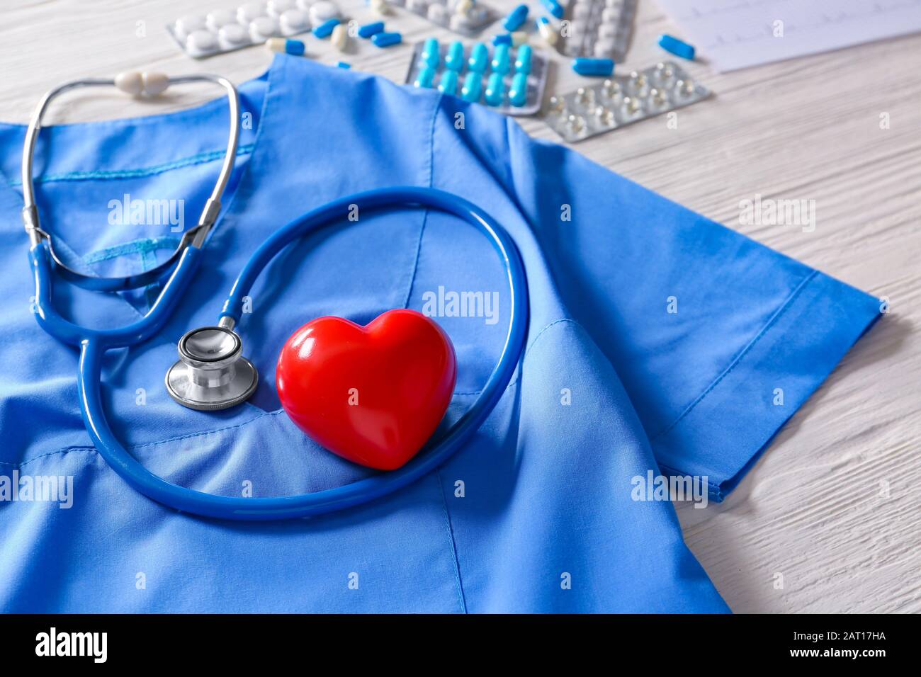 Stethoscope, doctor's uniform, heart and pills on wooden background ...