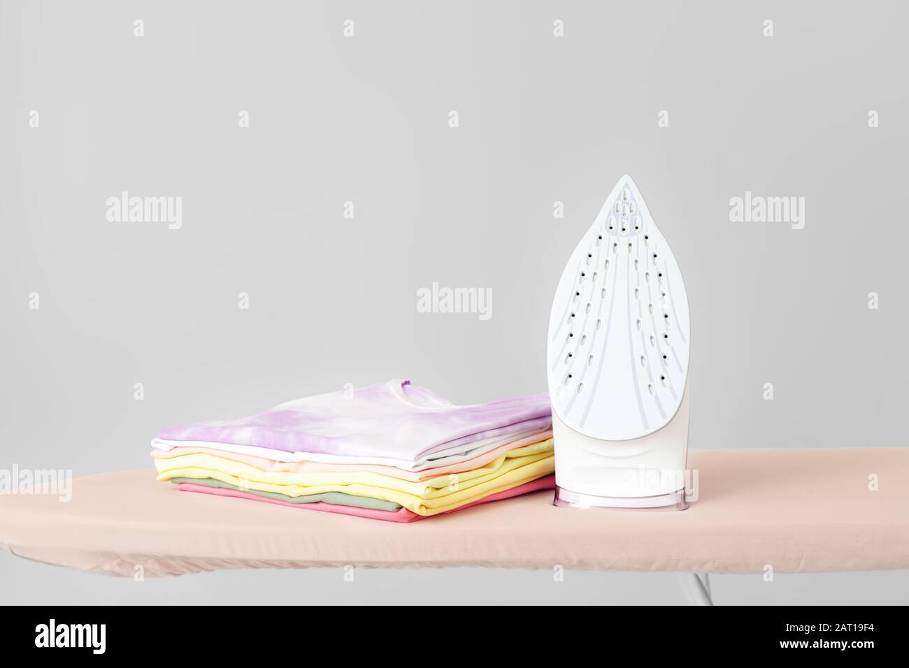 Iron and clean clothes on board against grey background Stock Photo - Alamy
