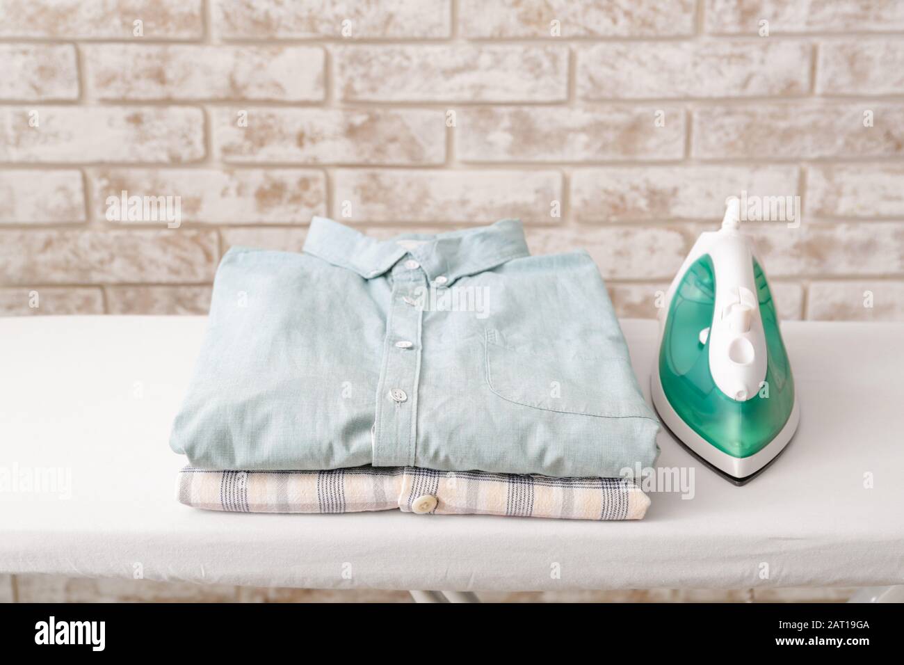 Iron and clean clothes on board against brick background Stock Photo ...