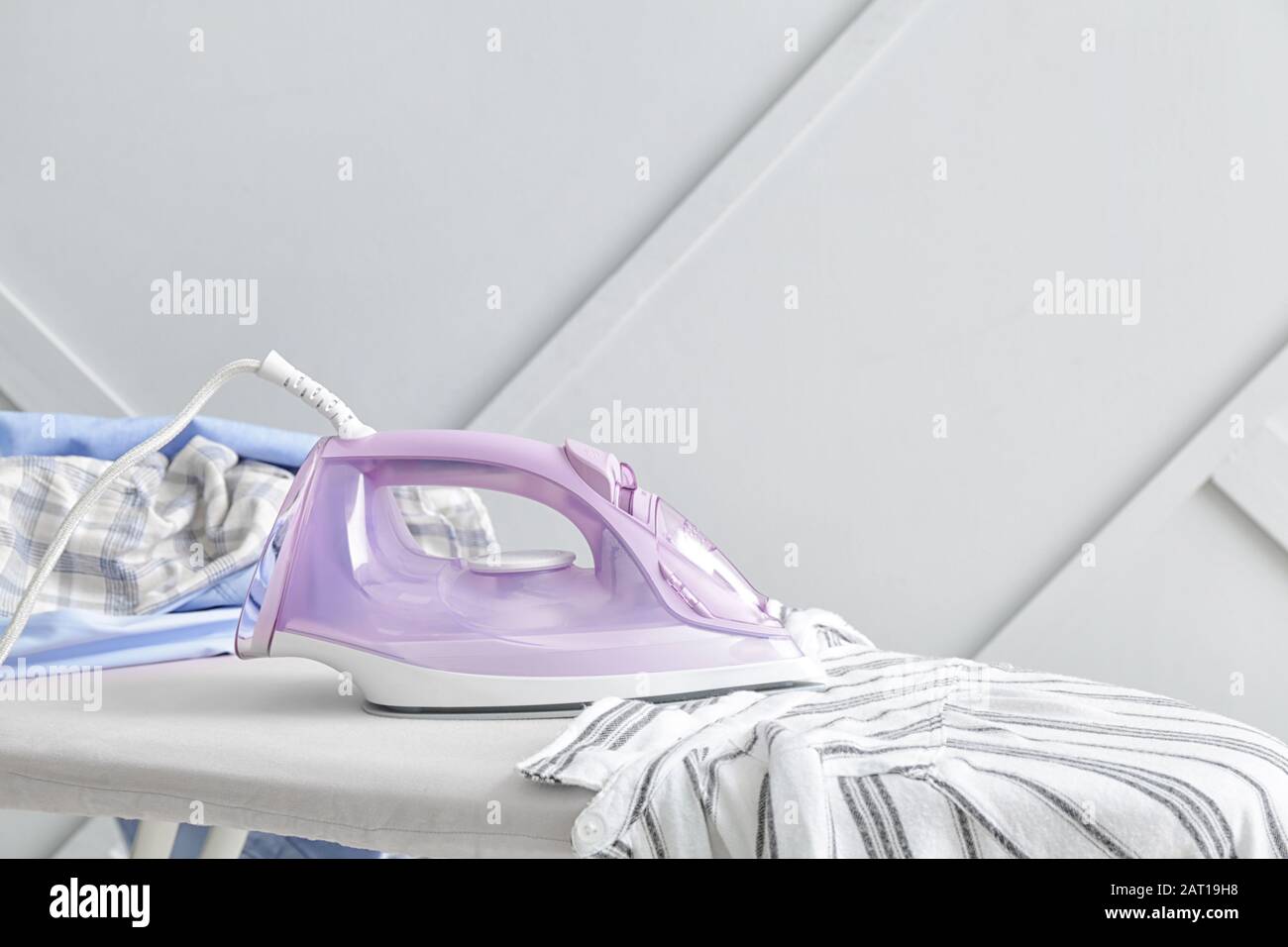 Iron and clean clothes on board against grey background Stock Photo - Alamy