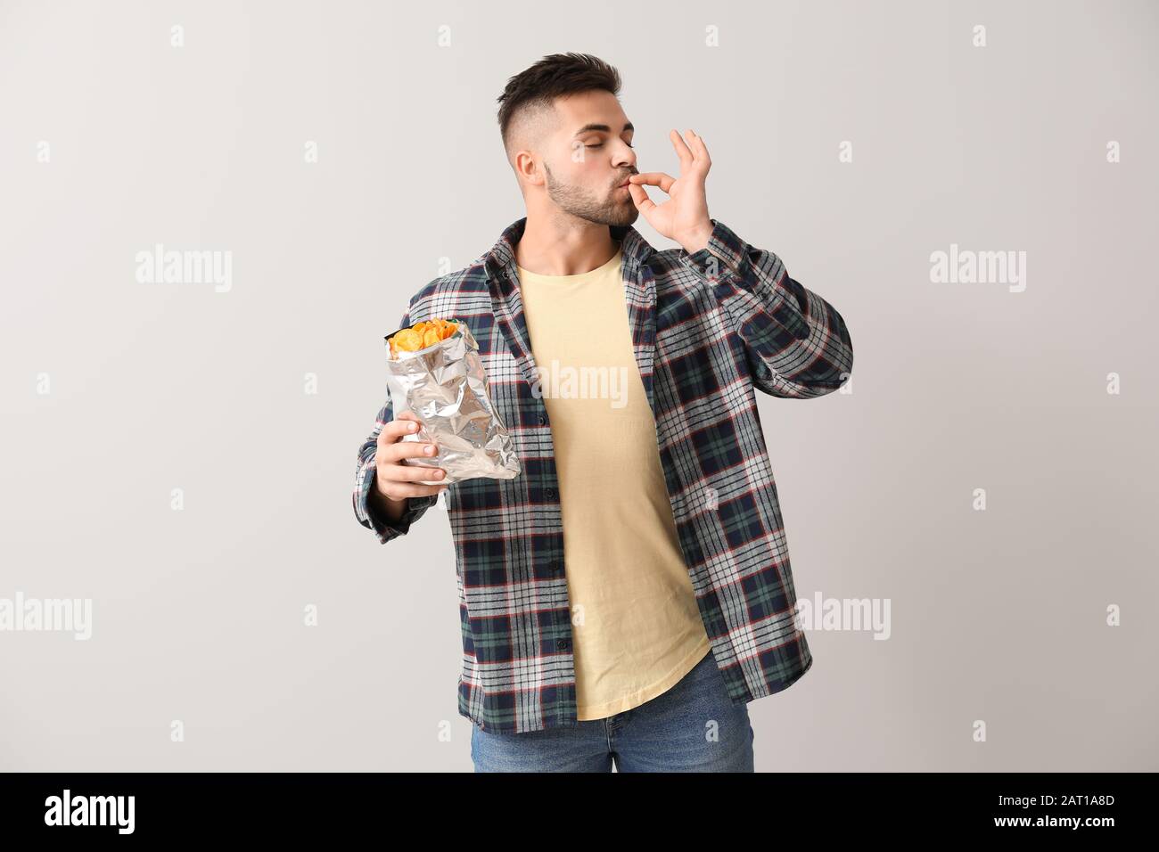 Handsome young man with tasty potato chips on light background Stock ...