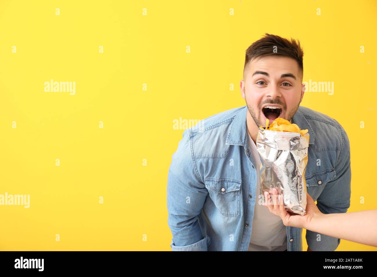 Handsome young man and hand with tasty potato chips on color background ...