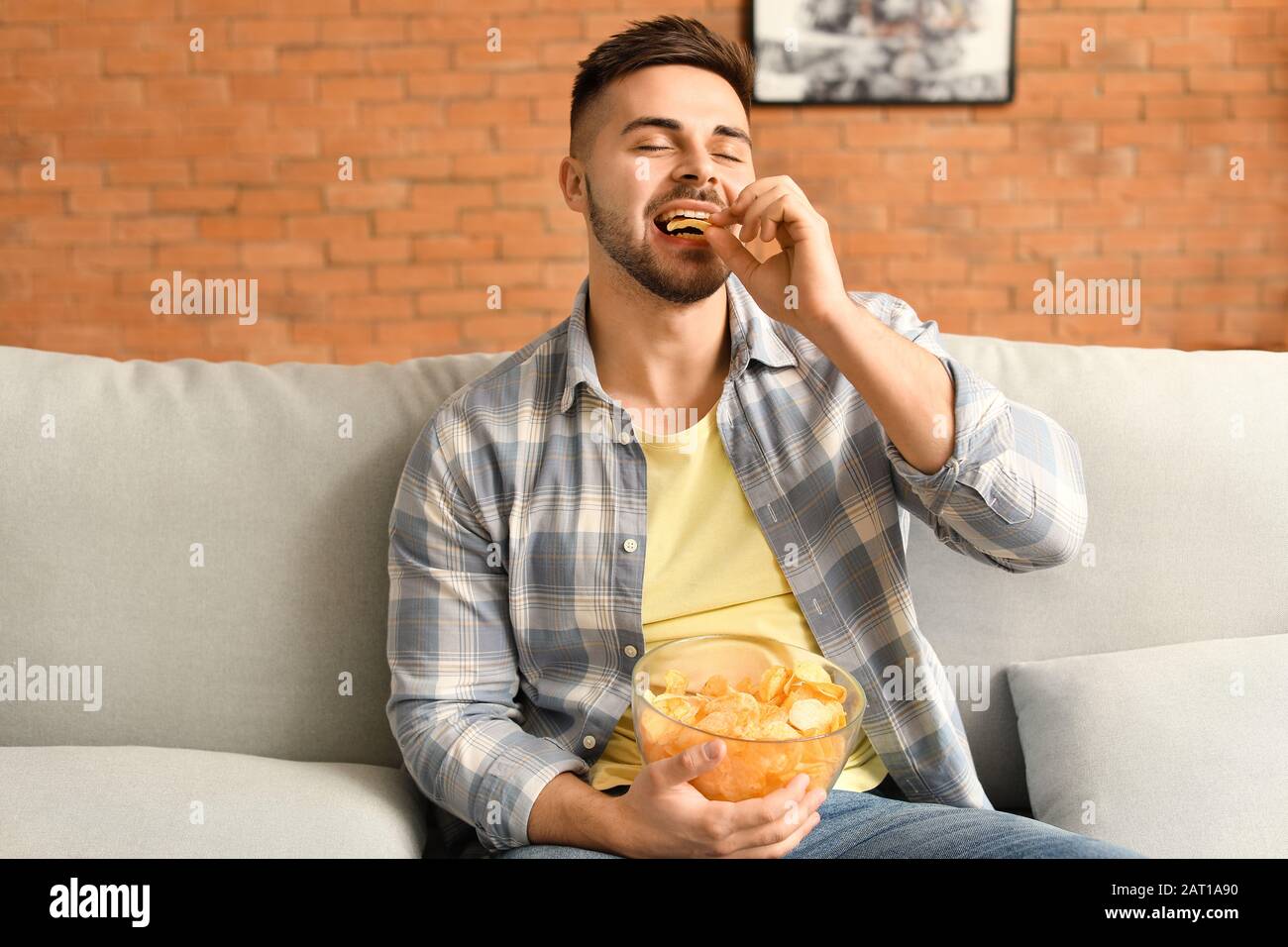 Handsome young man eating tasty potato chips at home Stock Photo - Alamy