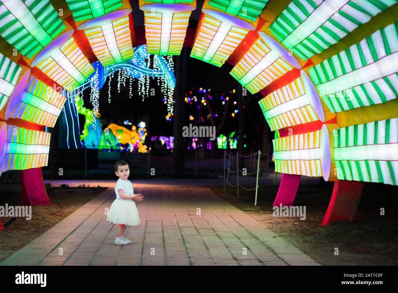 a cute little girl in the white dress in the Dubai Glow Garden at night ...
