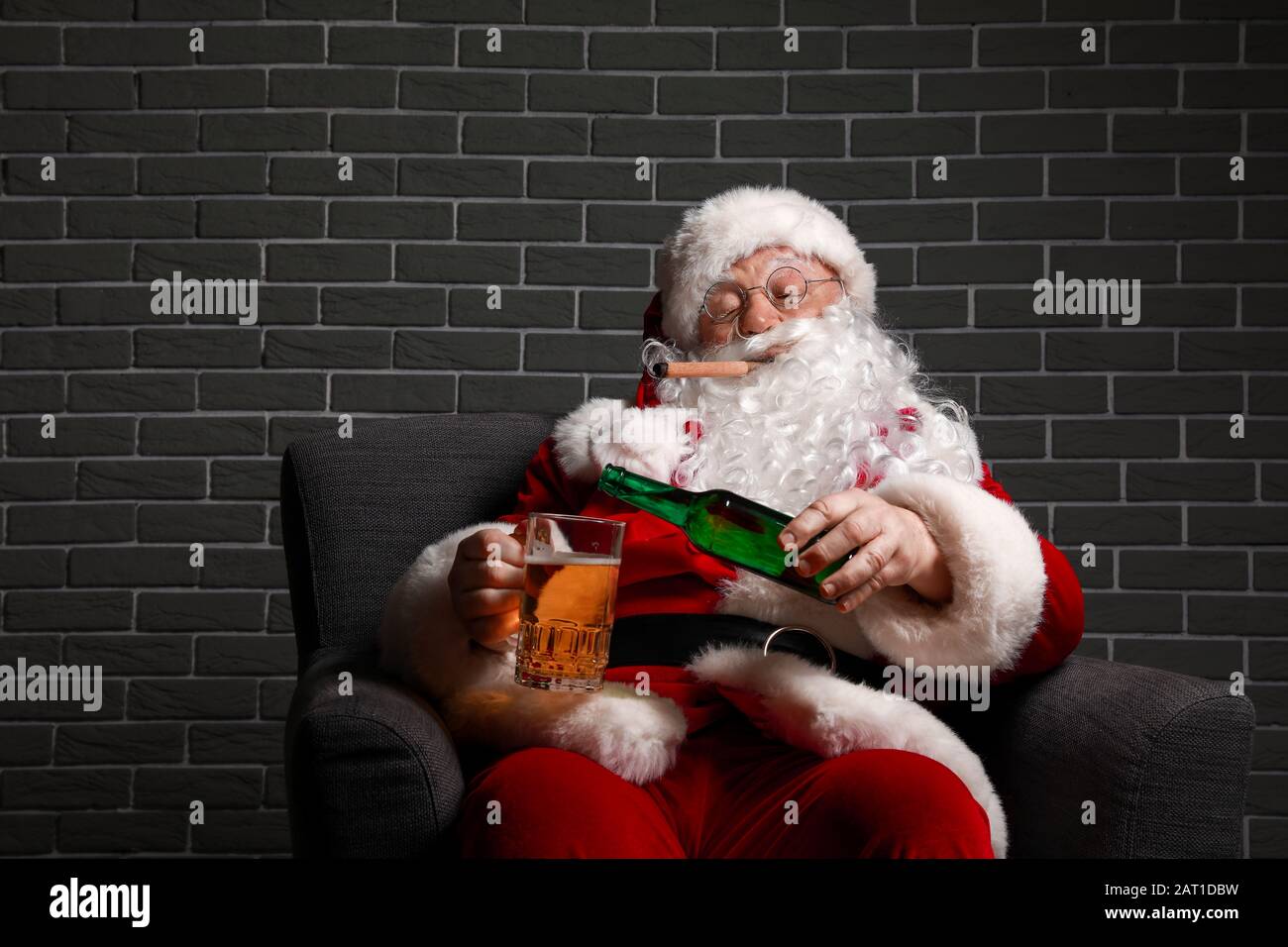 Funny drunk Santa Claus sitting in armchair against brick background Stock Photo - Alamy