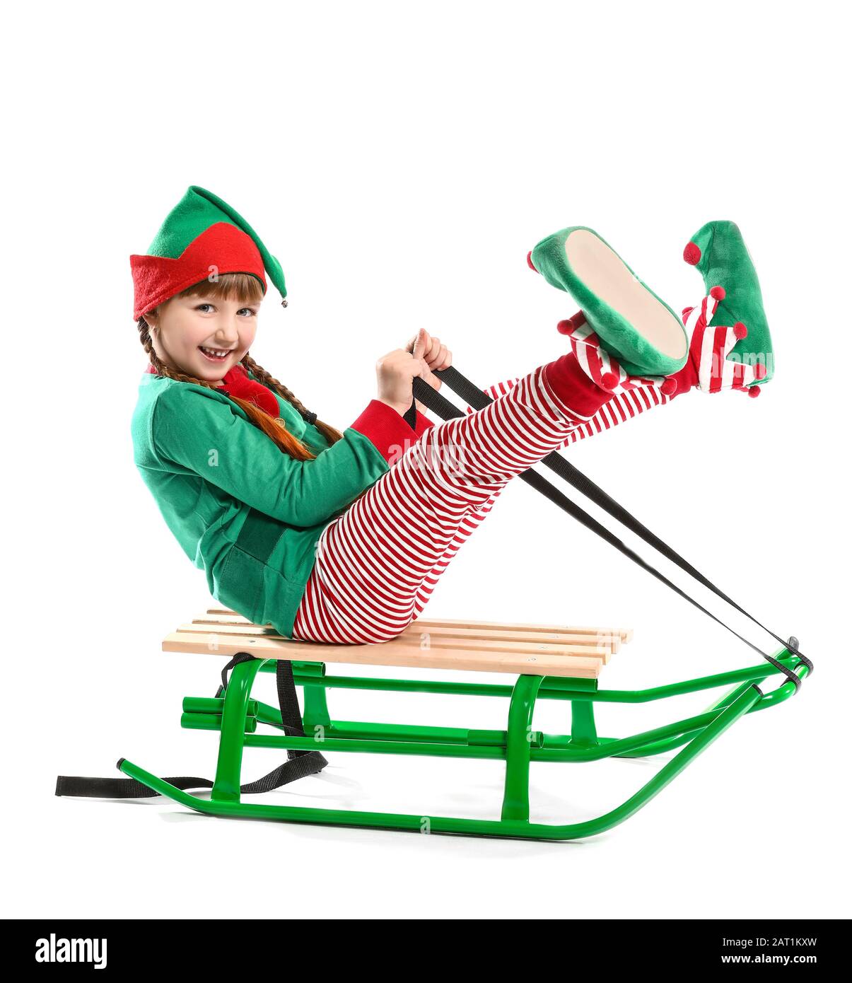 Little girl in costume of elf sitting on sledge against white ...