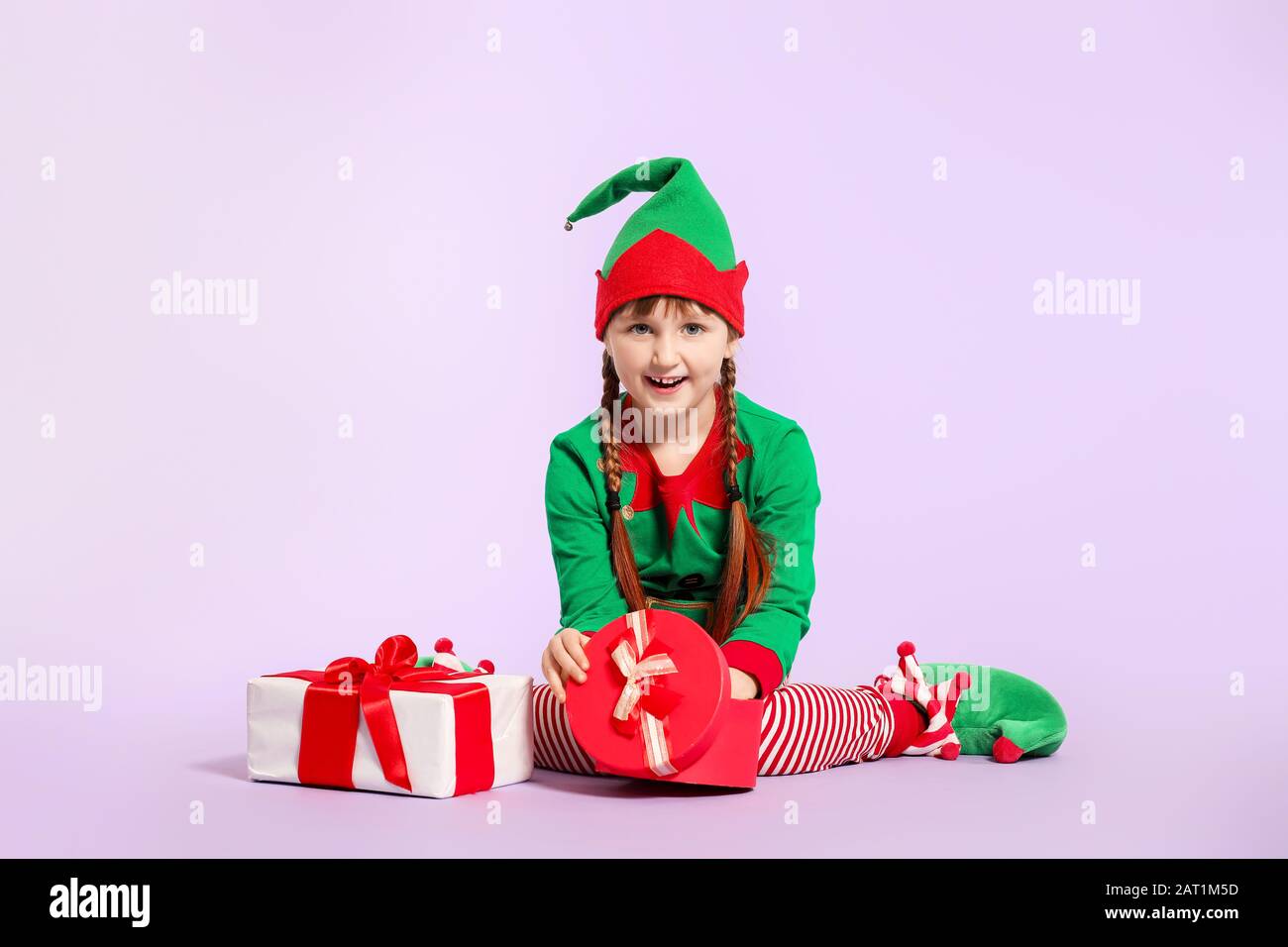 Little girl in costume of elf opening gift on color background Stock ...
