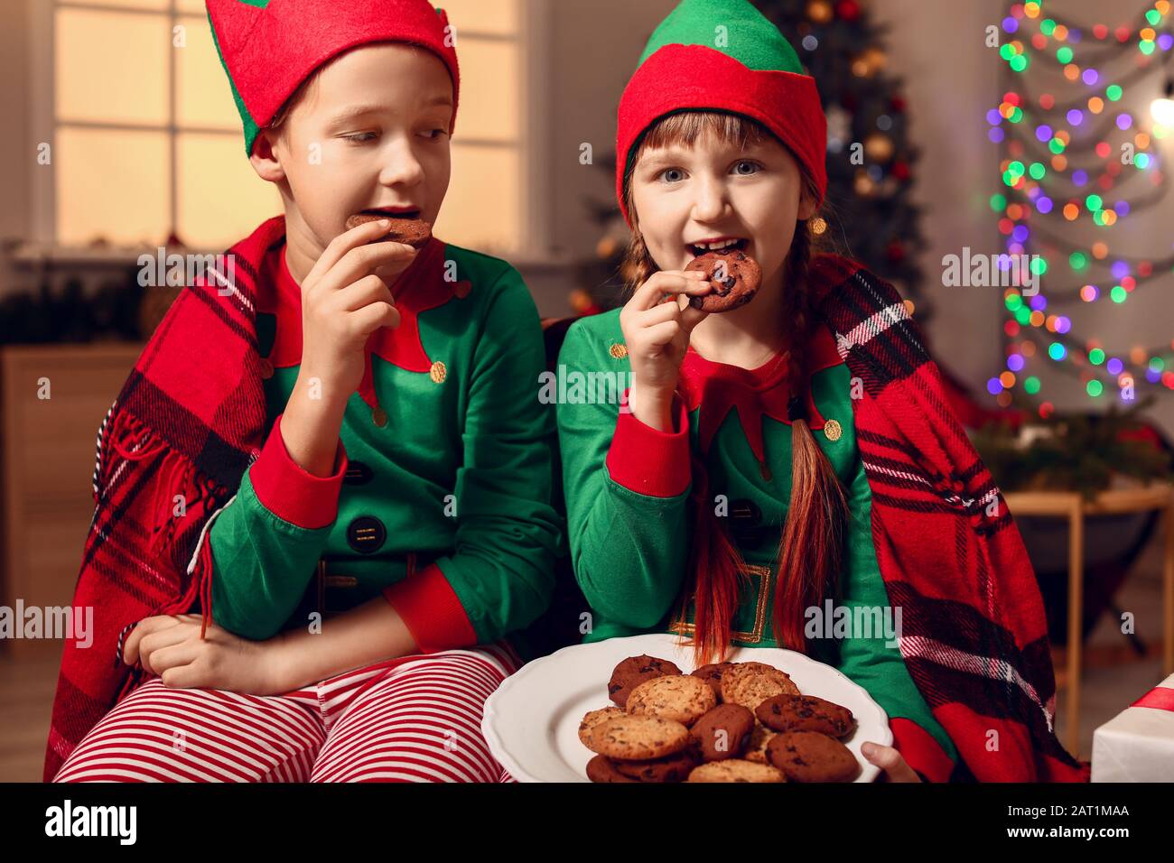 Little children in costume of elf eating cookies in room decorated for ...