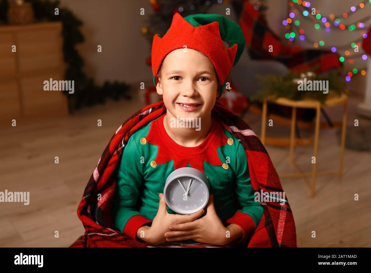 Little boy in costume of elf and with clock in room decorated for ...
