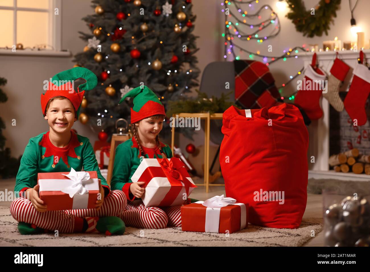 Little children in costume of elf and with gifts in room decorated for ...