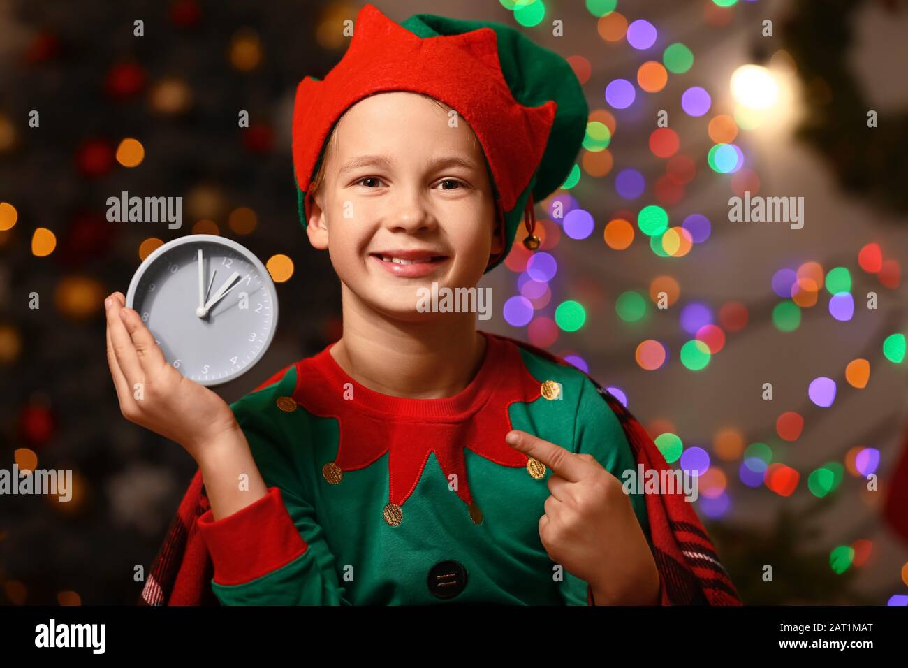 Little boy in costume of elf and with clock in room decorated for ...