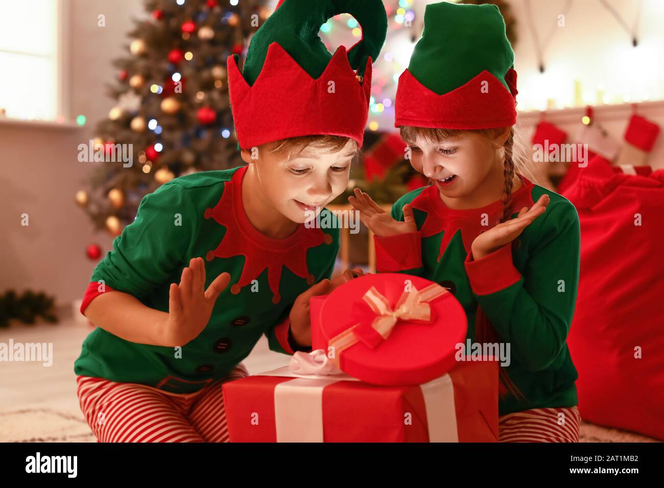 Little children in costume of elf opening gift in room decorated for ...