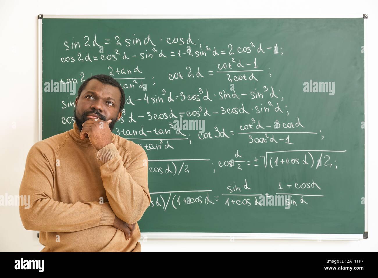 Thoughtful African-American math teacher near blackboard in classroom ...