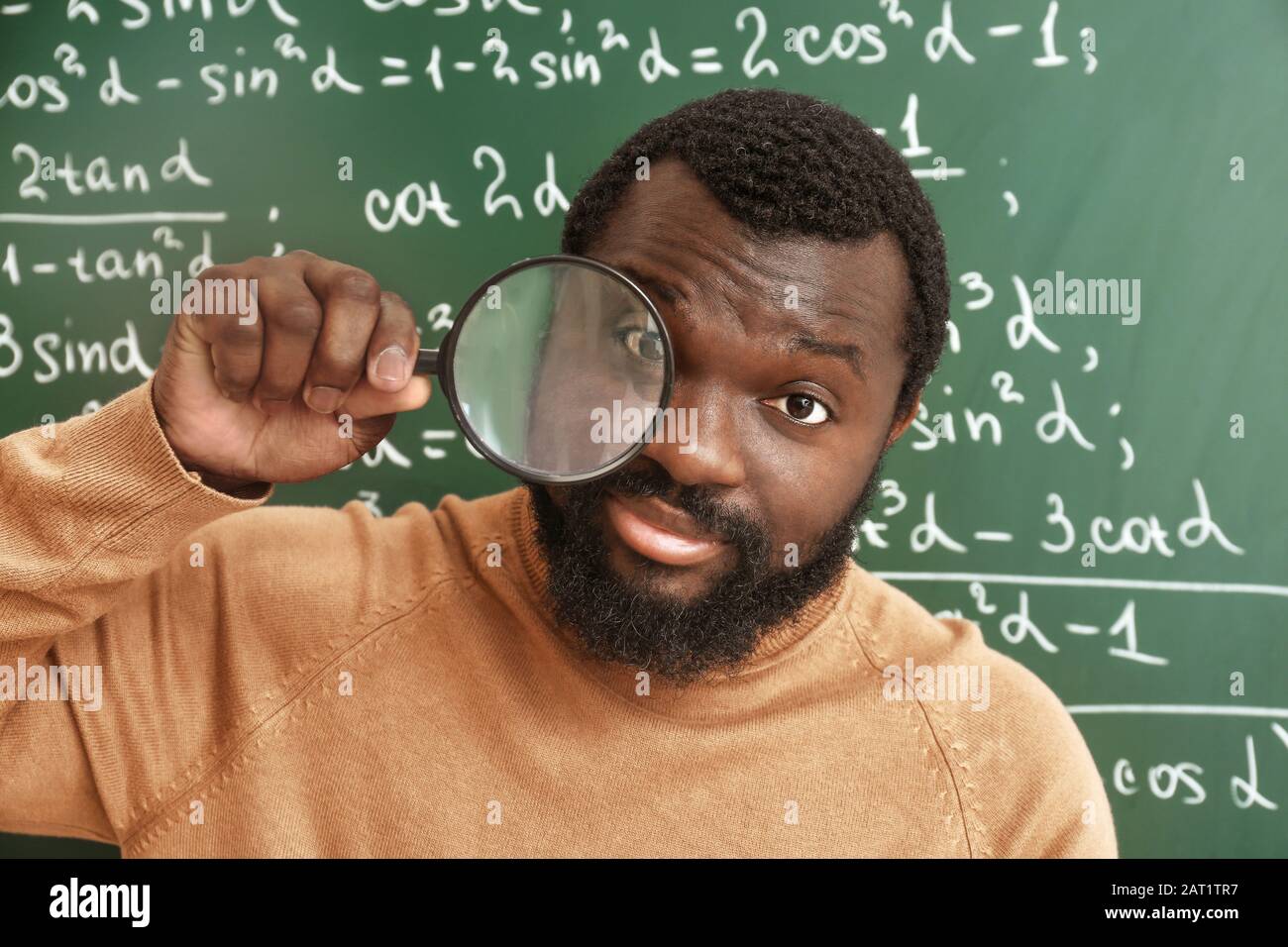 African-American math teacher with magnifier near blackboard in ...
