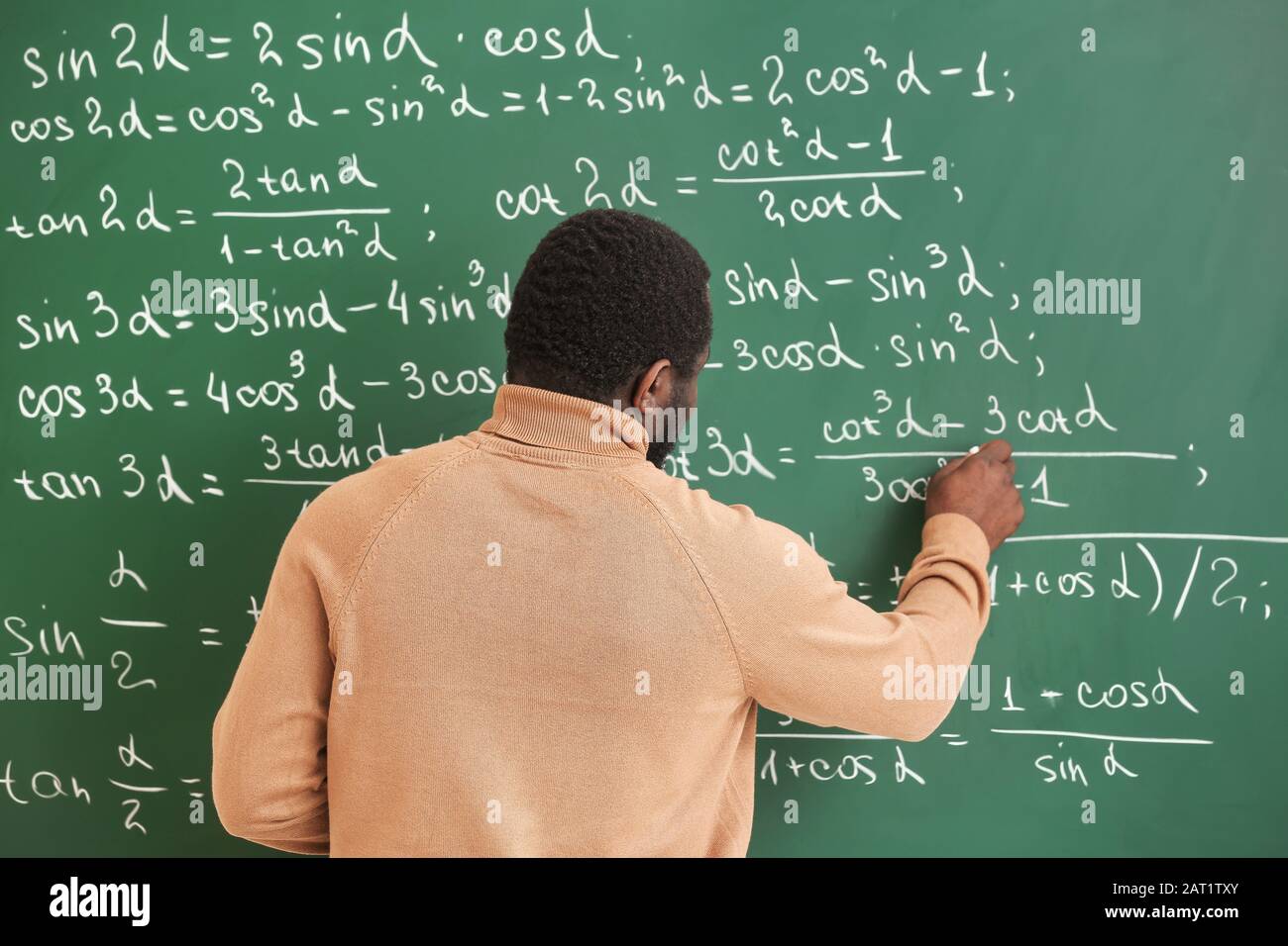 African-American math teacher writing on blackboard in classroom Stock ...