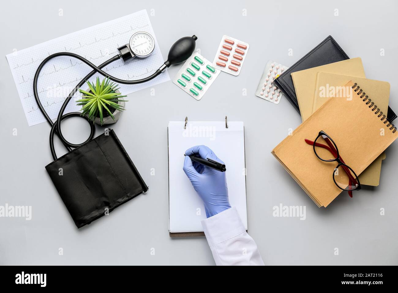 Hand of doctor writing in notebook, sphygmomanometer and pills on light ...
