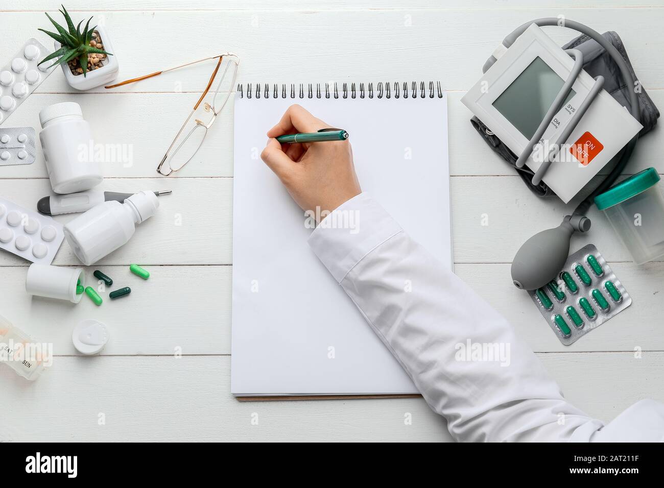 Hand of doctor writing in notebook, sphygmomanometer and pills on white ...