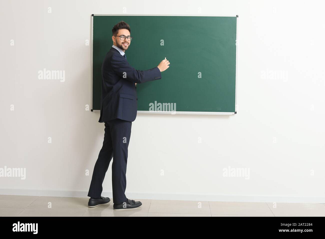 Male teacher writing on blackboard in classroom Stock Photo - Alamy