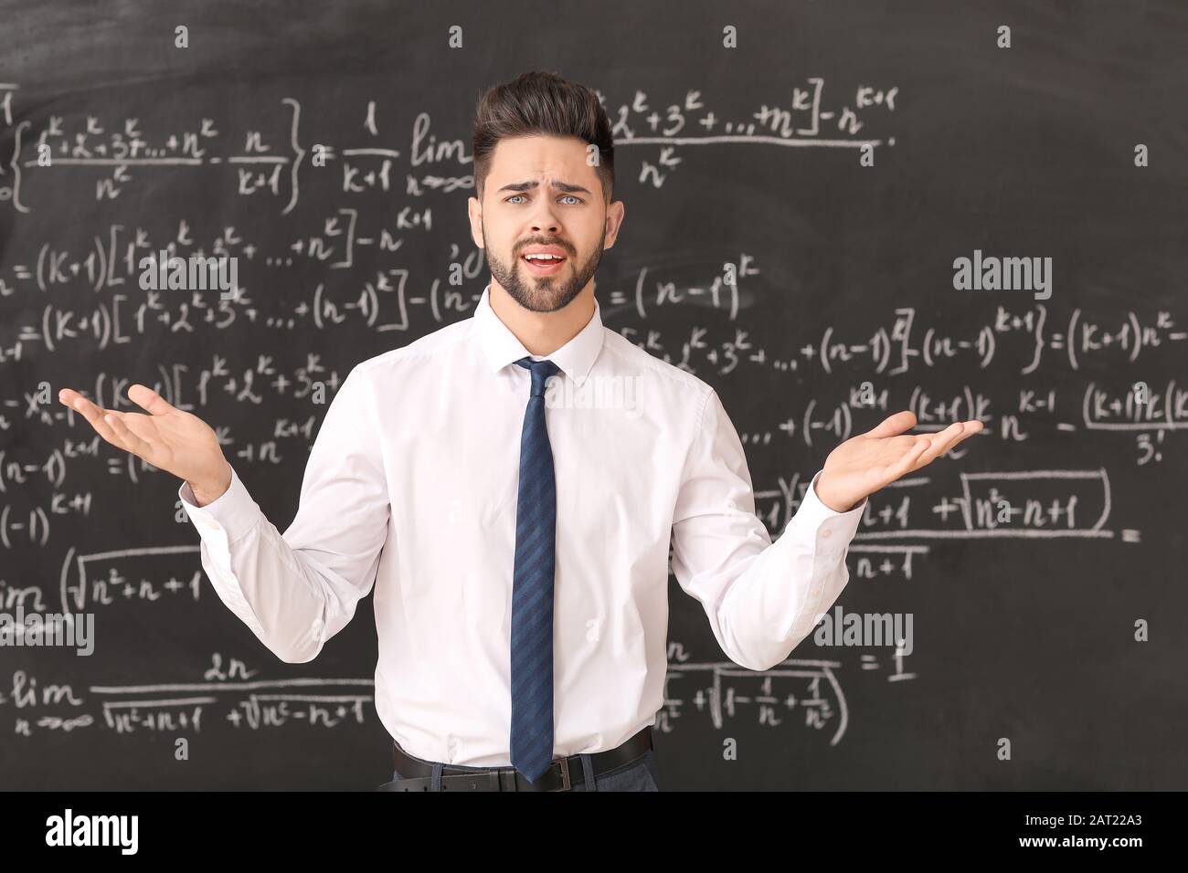 Confused male teacher near blackboard in classroom Stock Photo - Alamy