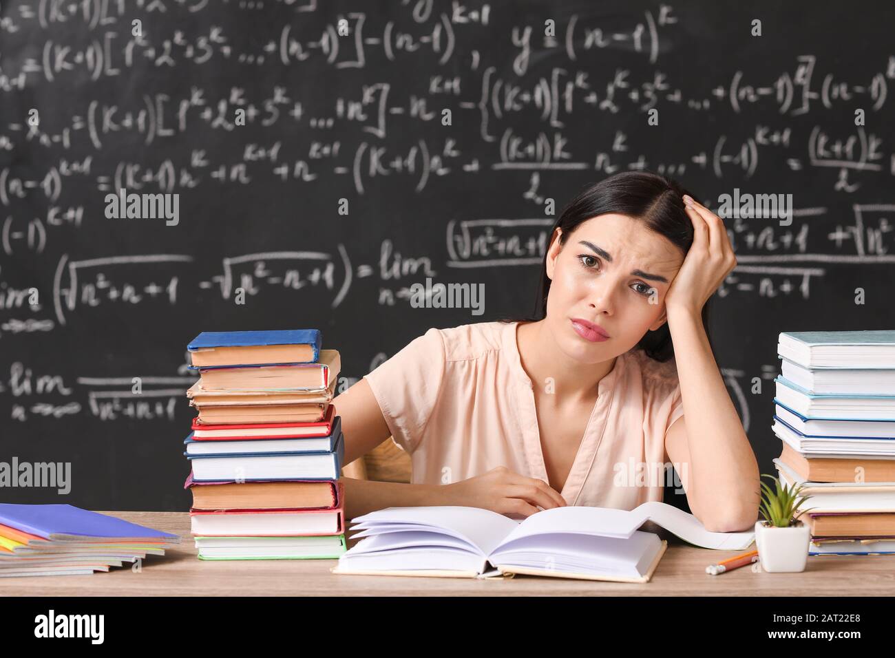 Tired female teacher at table in classroom Stock Photo - Alamy