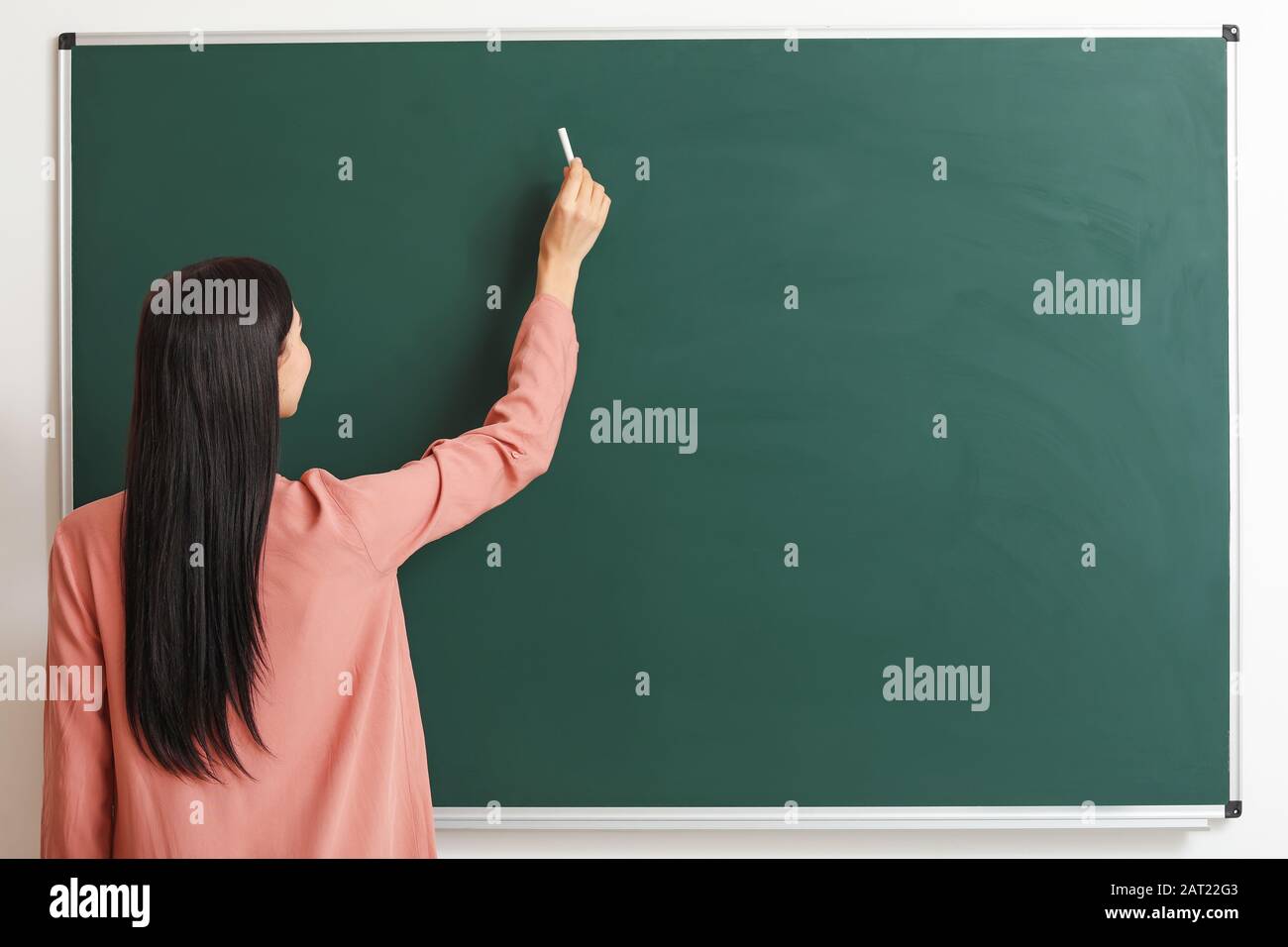 Female teacher writing on blackboard in classroom Stock Photo - Alamy