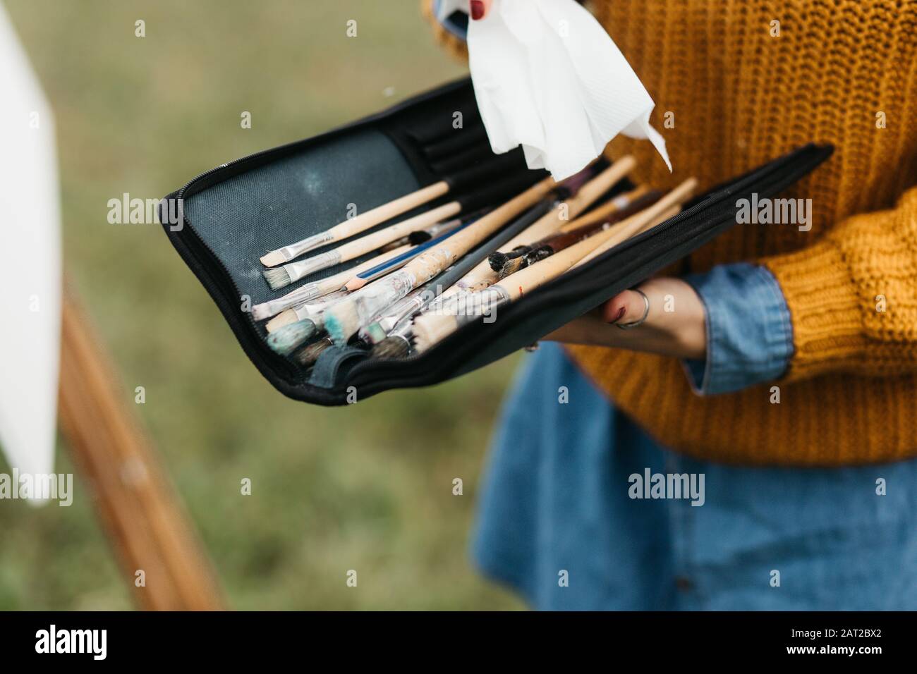 Close up photo of young female artist working on painting outdoors. She holds oil paints, artist ...