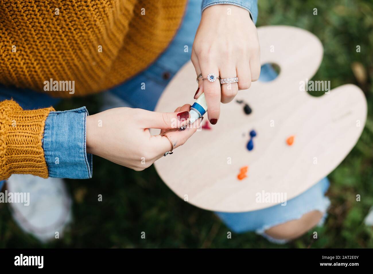 Close up photo of young female artist working on painting outdoors. She holds oil paints, artist ...