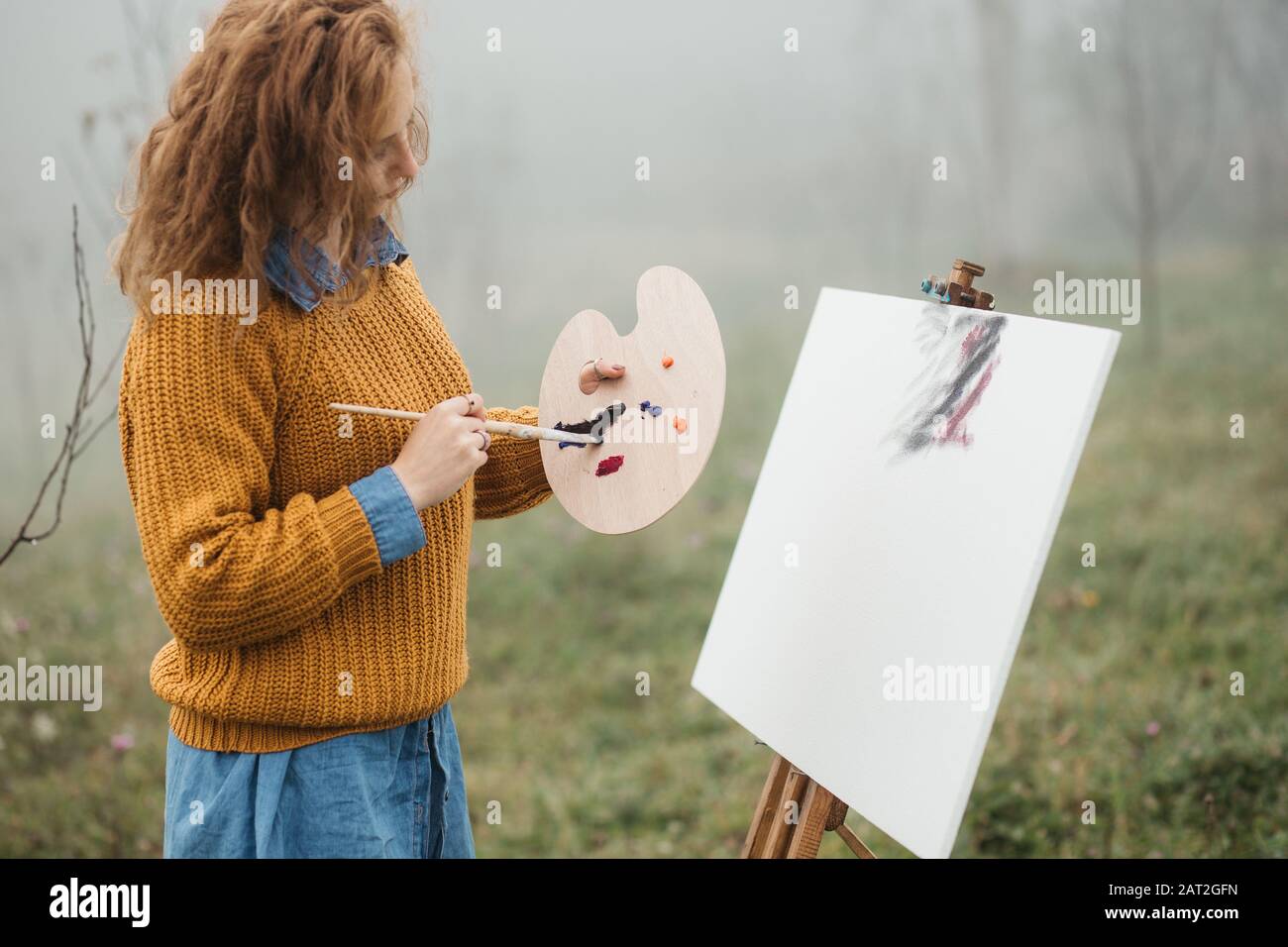Young female artist working on painting outdoors. She is in front of ...