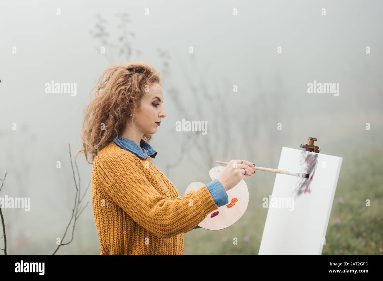 Young female artist working on painting outdoors. She is in front of ...
