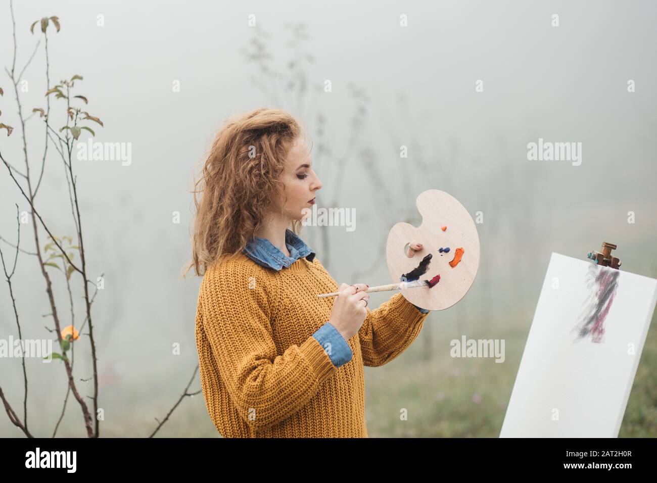 Young female artist working on painting outdoors. She is in front of ...