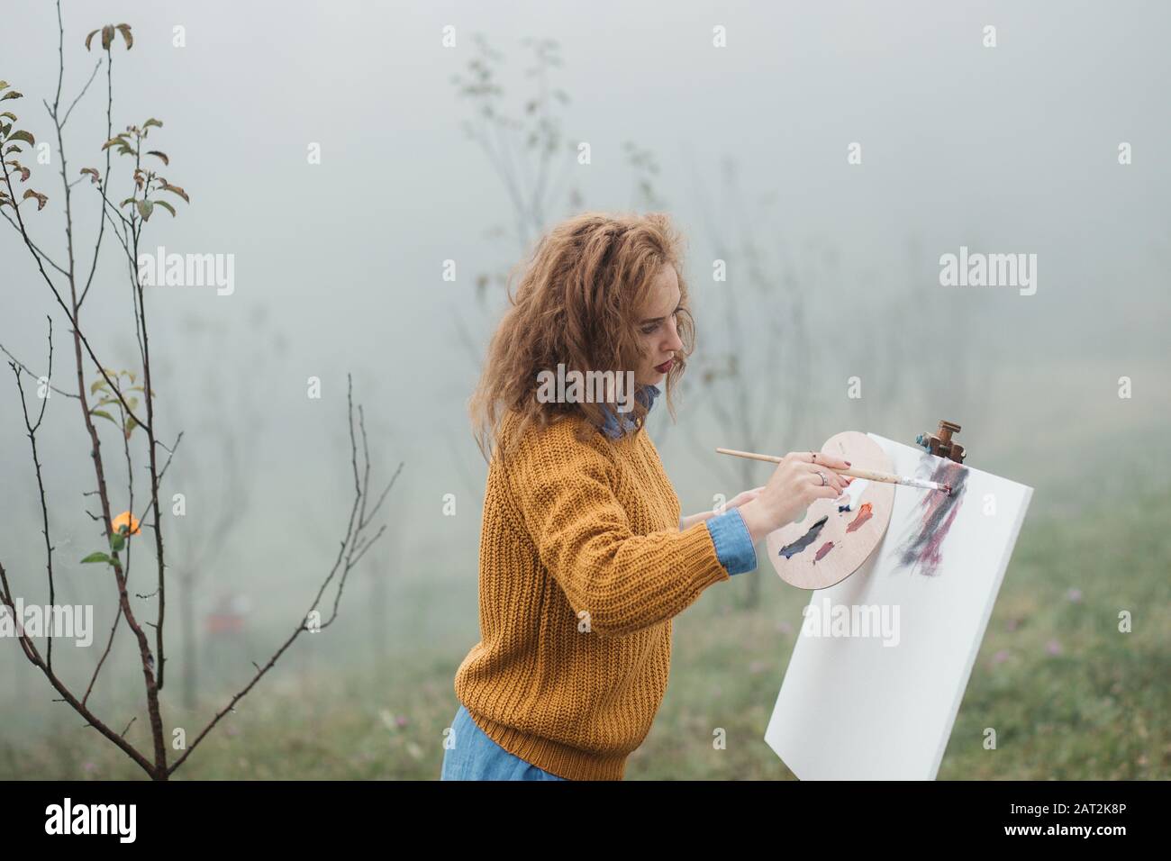Young female artist working on painting outdoors. She is in front of ...