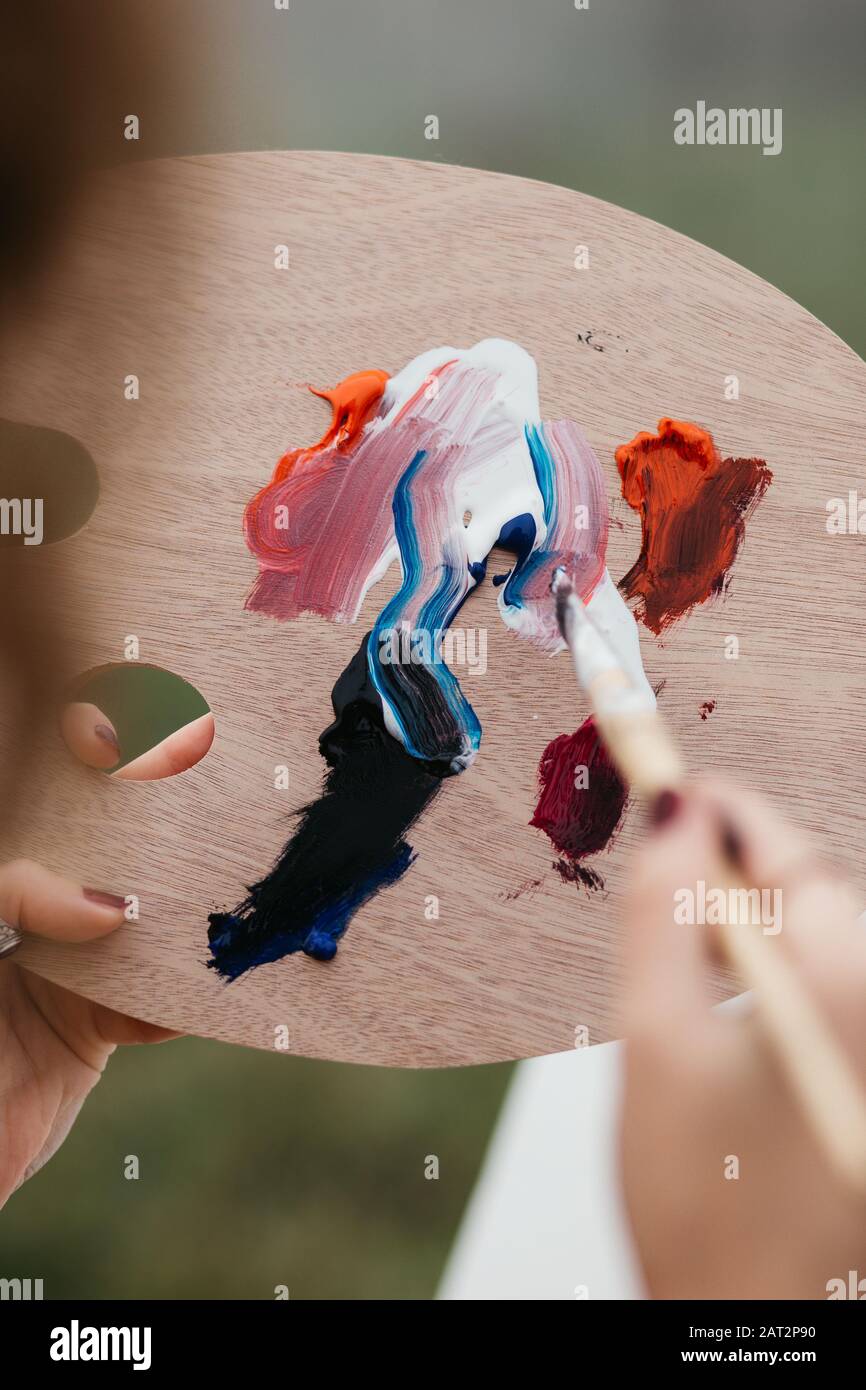 Close up photo of young female artist working on painting outdoors. She holds oil paints, artist ...