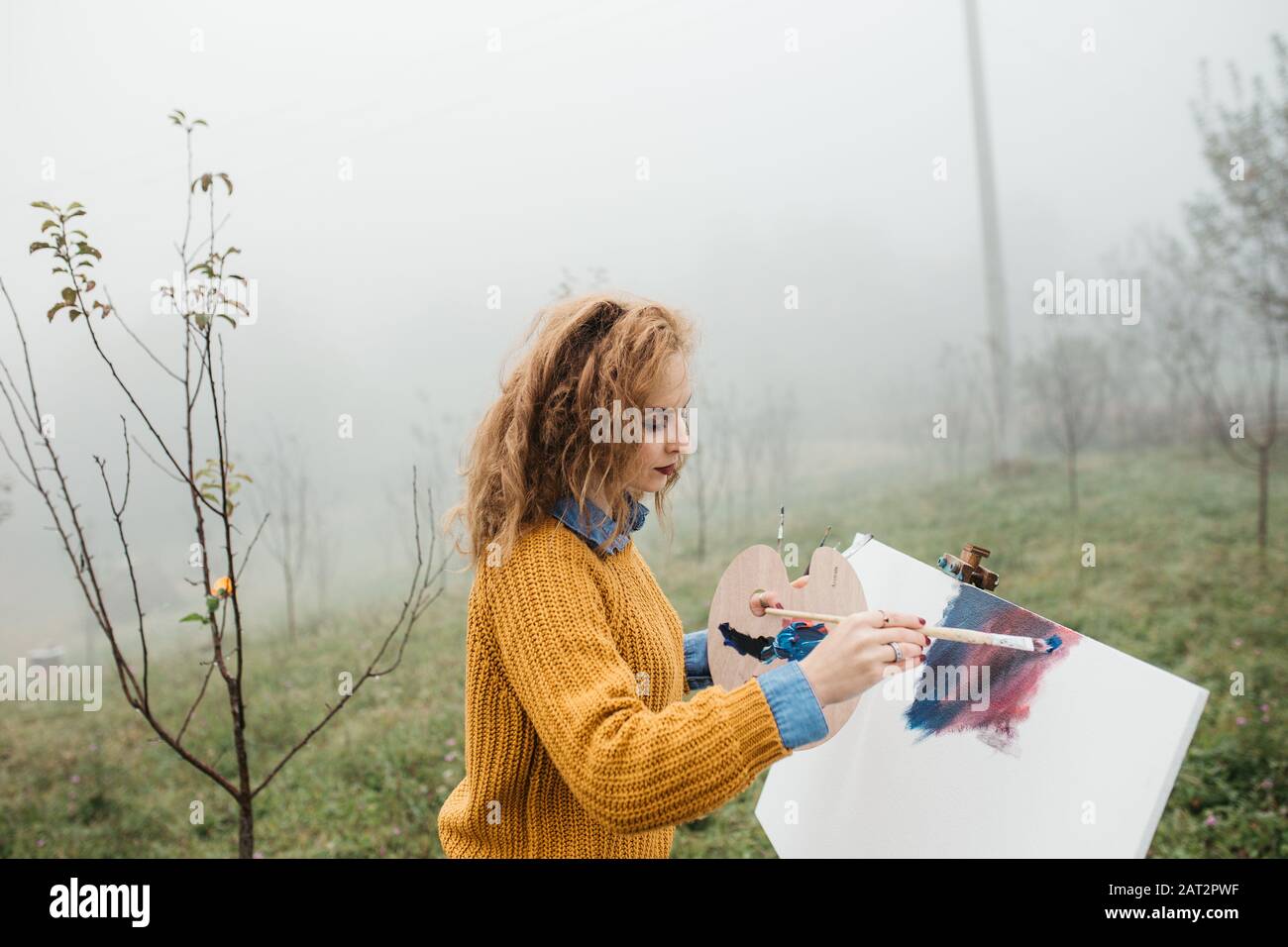Young female artist working on painting outdoors. She is in front of ...