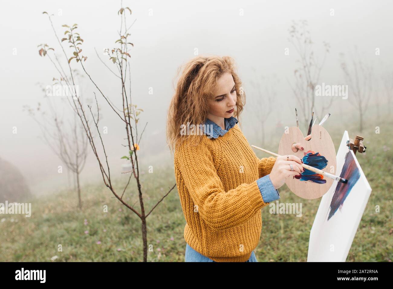 Young female artist working on painting outdoors. She is in front of ...