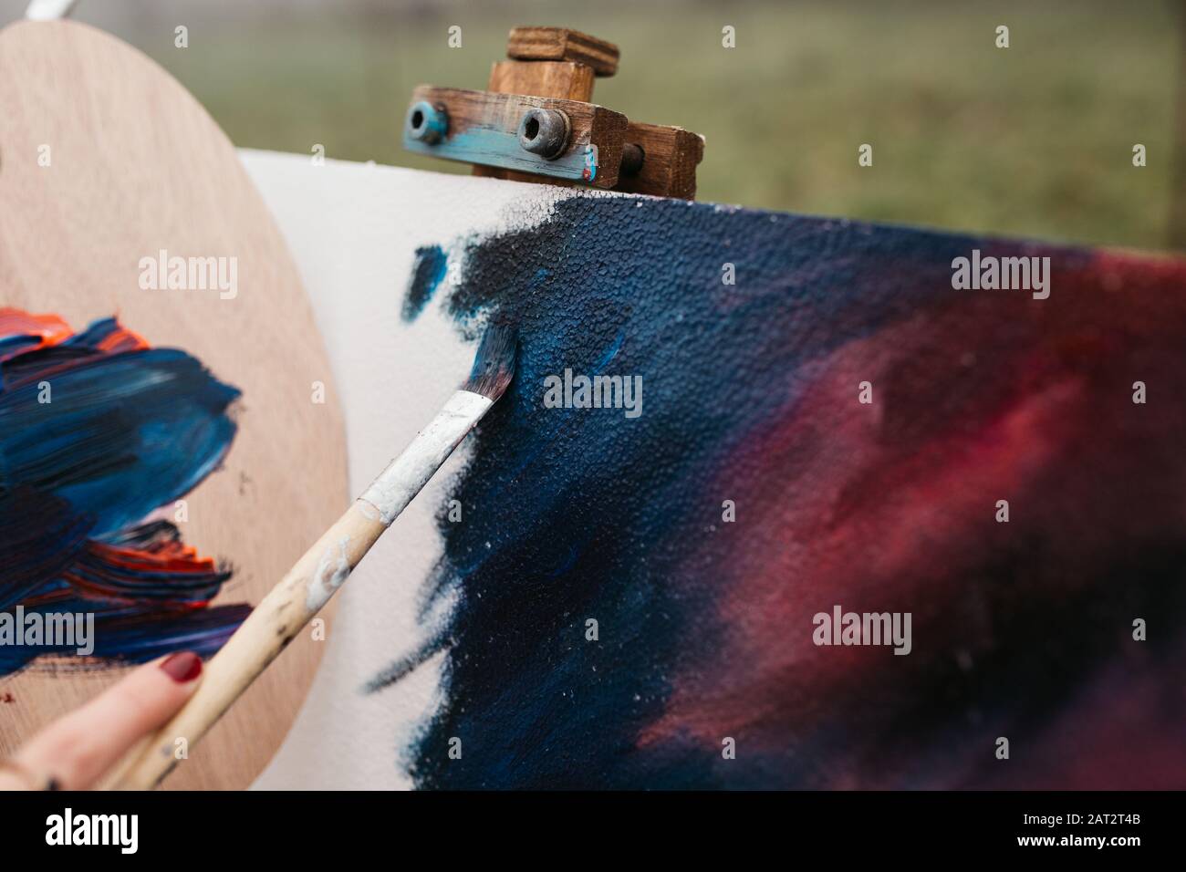 Close up photo of young female artist working on painting outdoors. She holds oil paints, artist ...