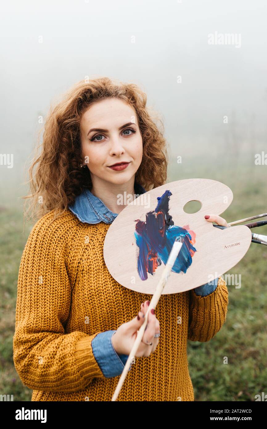 Young female artist working on painting outdoors. She is in front of ...
