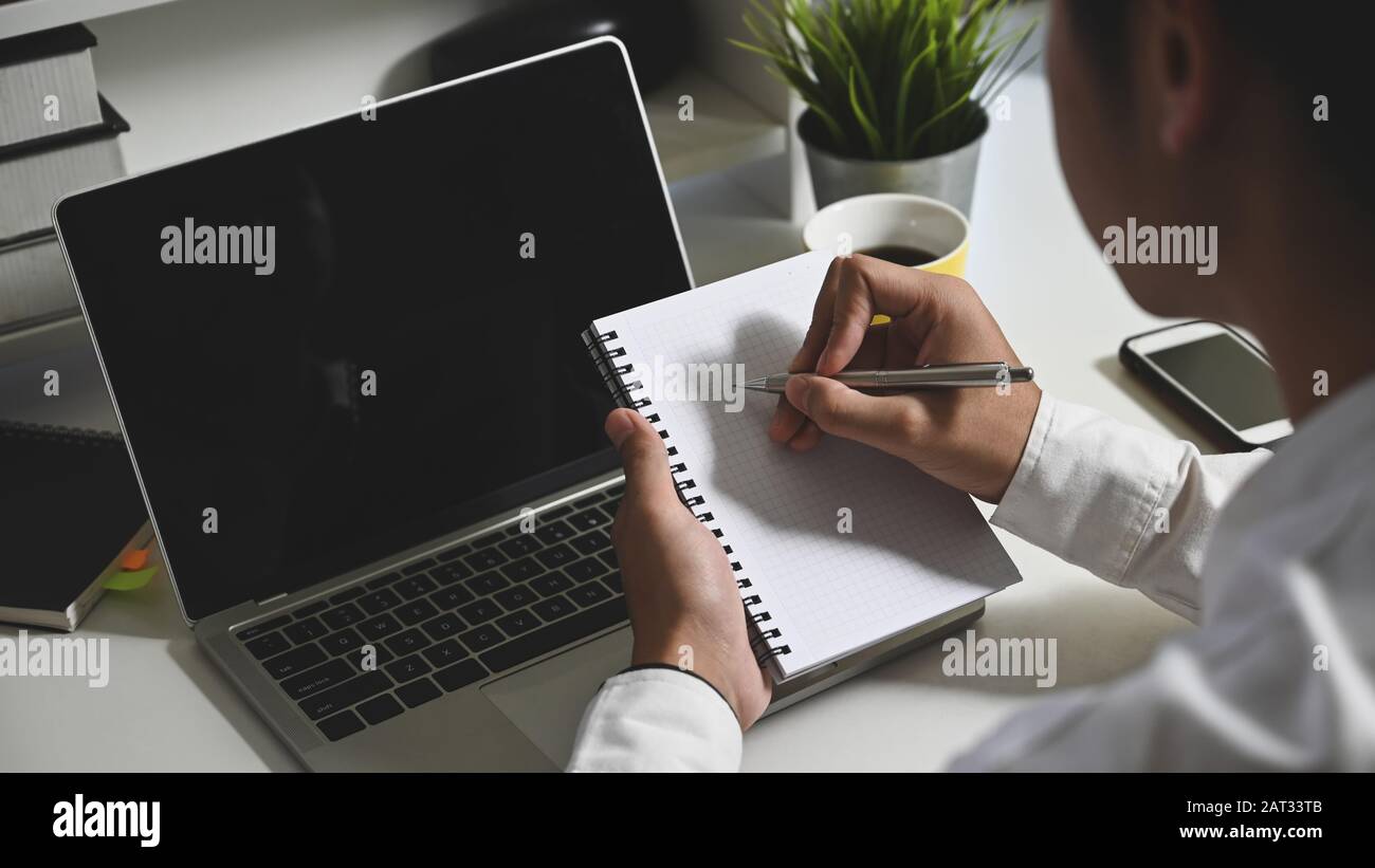 Closeup business man taking notes in front black blank screen laptop at ...