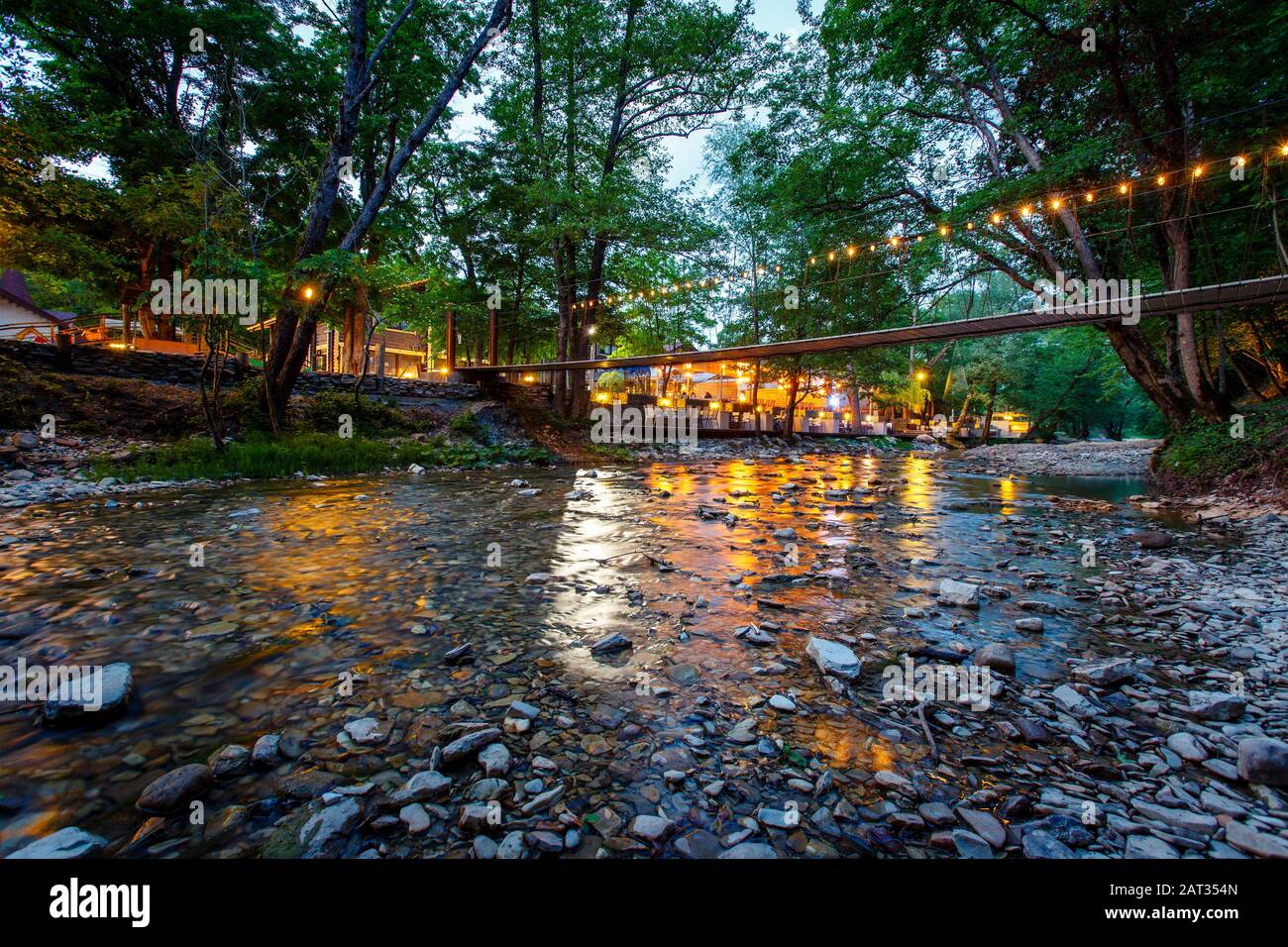 a small pedestrian suspension bridge over a shallow mountain river ...