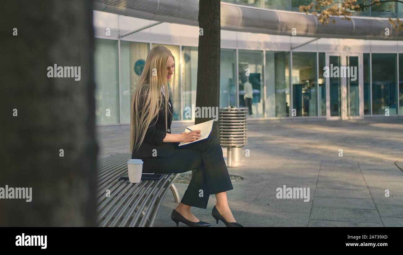 Side view of elegant businesswoman sitting on bench in patio and ...