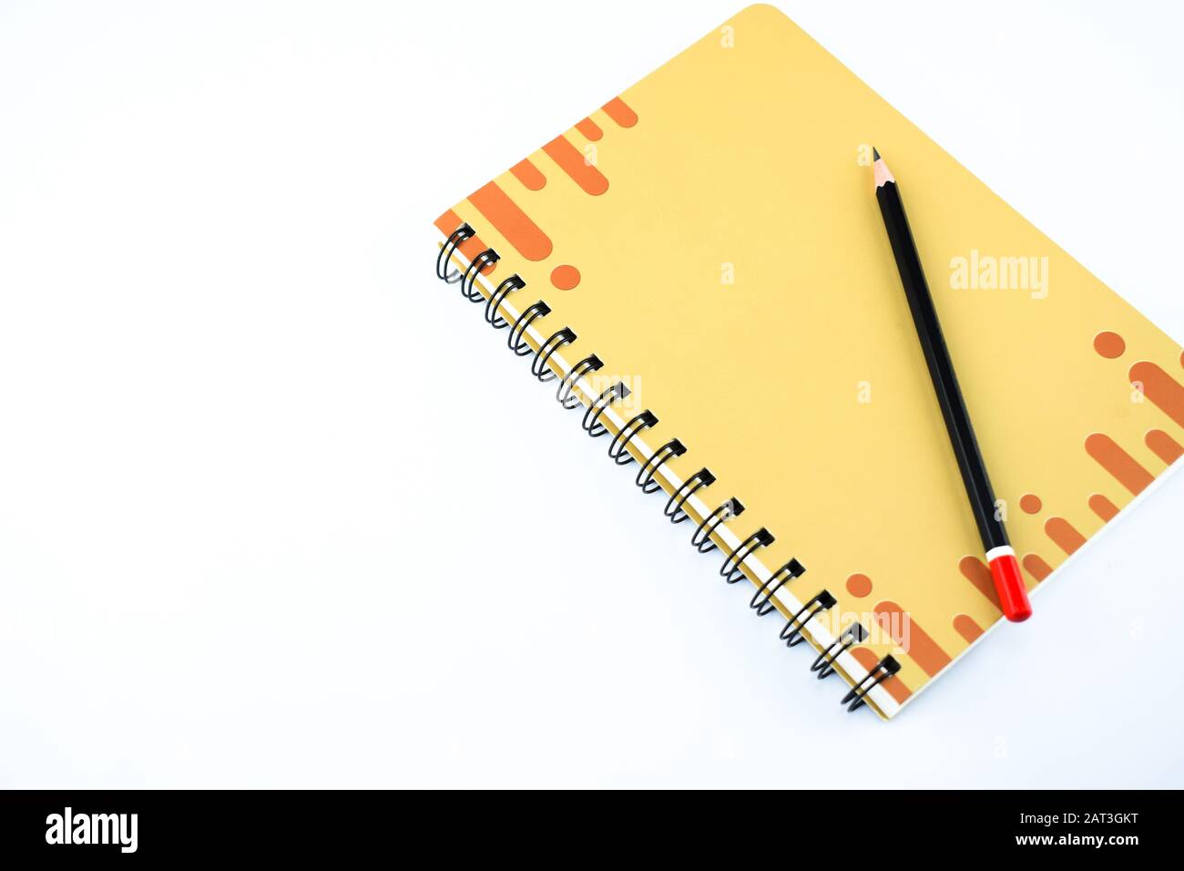 A dark black pencil on a designed orange notebook with a isolated white ...