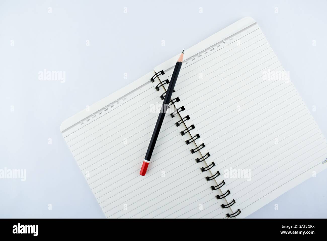 A dark black wooden pencil over a notebook on a isolated white ...