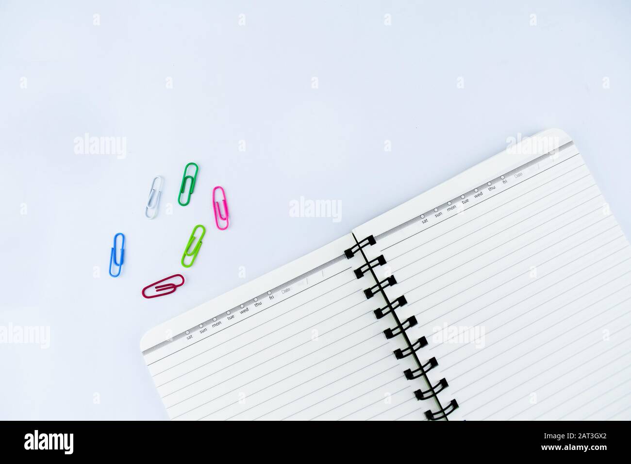 A white notebook along side some different colored paper clips on an ...