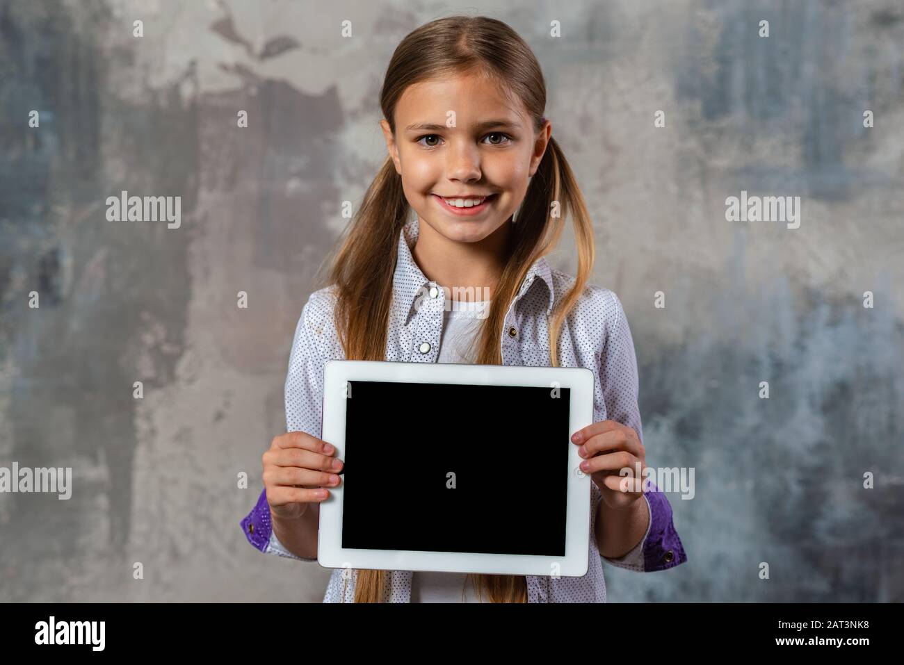 Smiling blonde girl holding ipad in her hands and looking at the camera ...